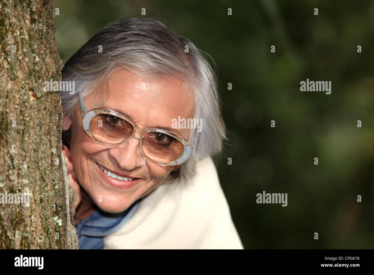 Elderly woman behind tree trunk Stock Photo - Alamy