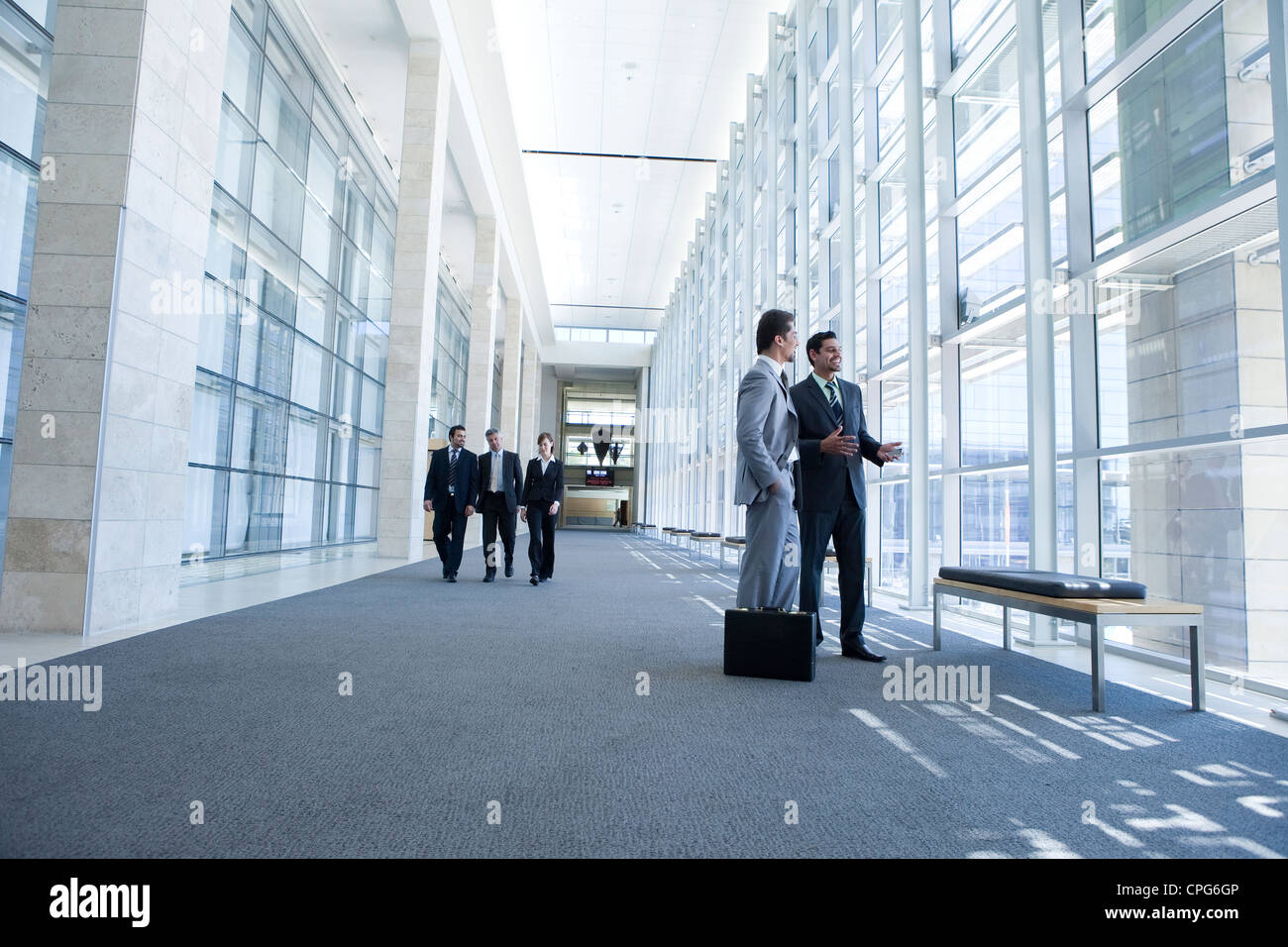 Two businessmen talking in office hallway. Three business people ...