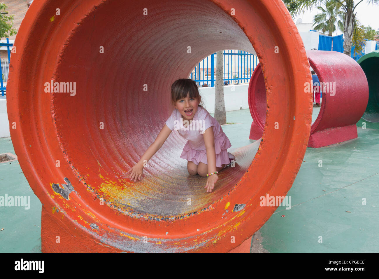 Four year old girl crawling through orange coloured concrete tunnel in ...