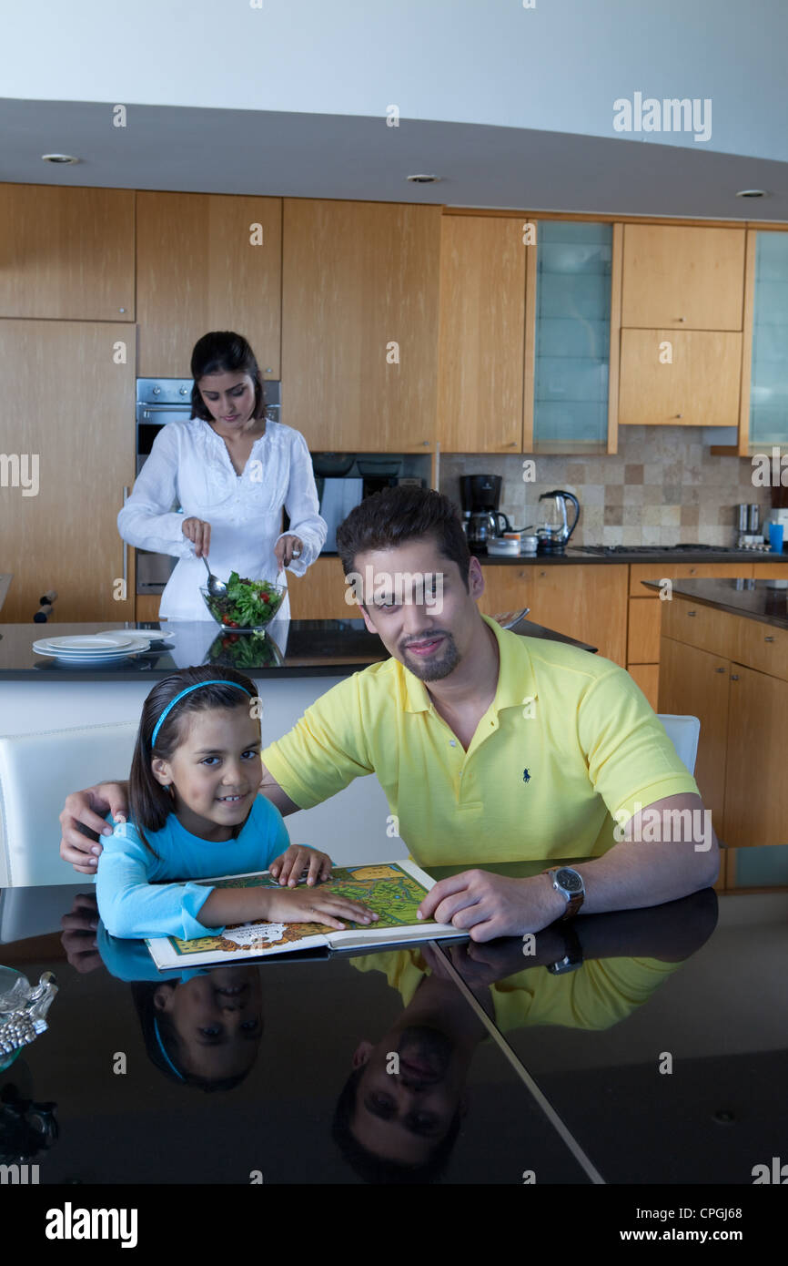 Father and daughter reading book in the dining table, mother preparing ...