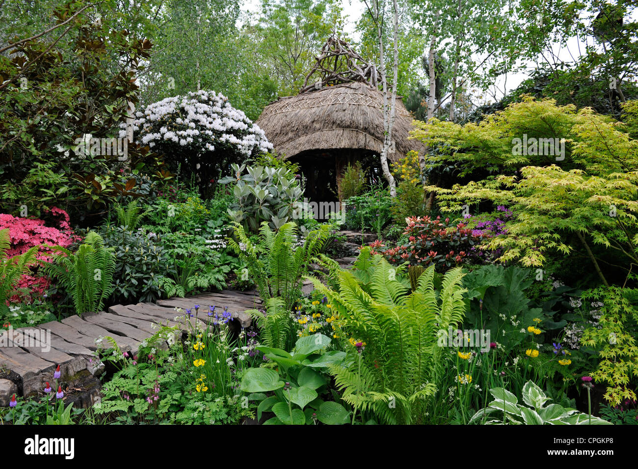 Mature show garden with thatch roofed hut at the RHS Chelsea flower ...
