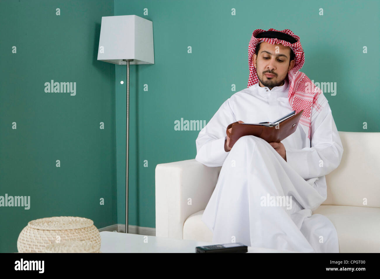 Arab man sitting on sofa, writing Stock Photo - Alamy