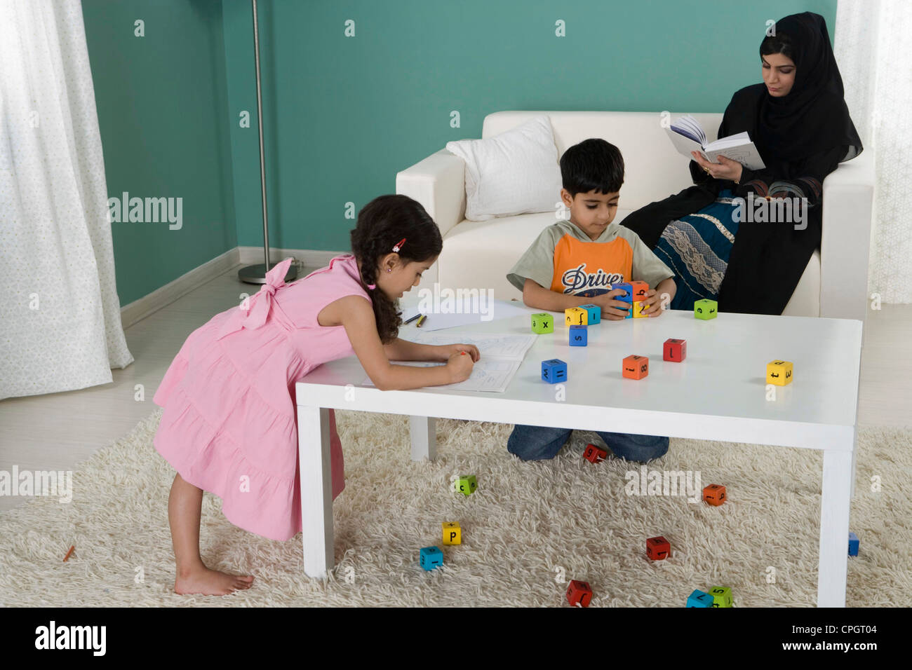 Arab mother reading, children playing at home Stock Photo - Alamy