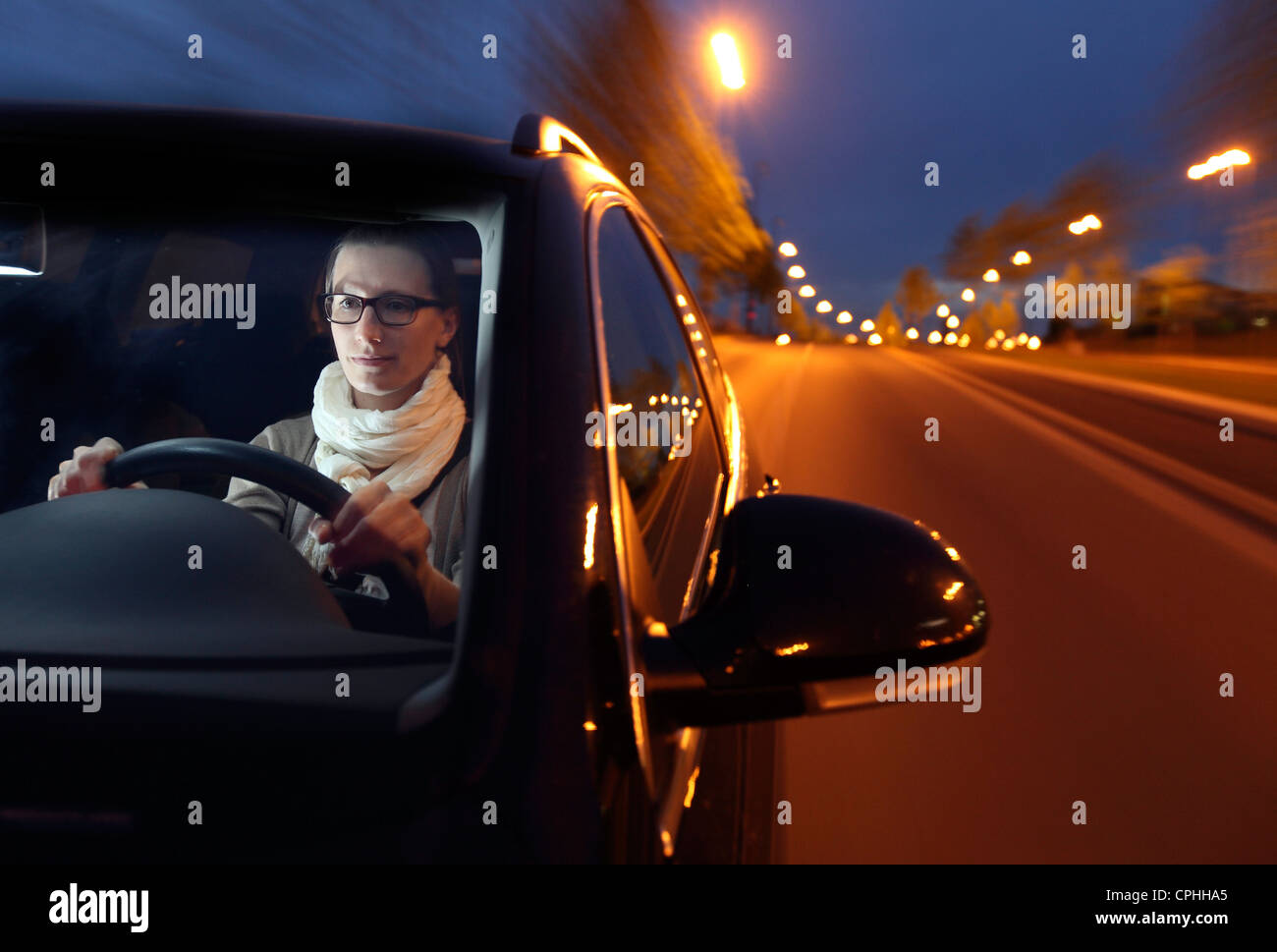 Young woman is driving a car at night, through a city, illuminated with ...