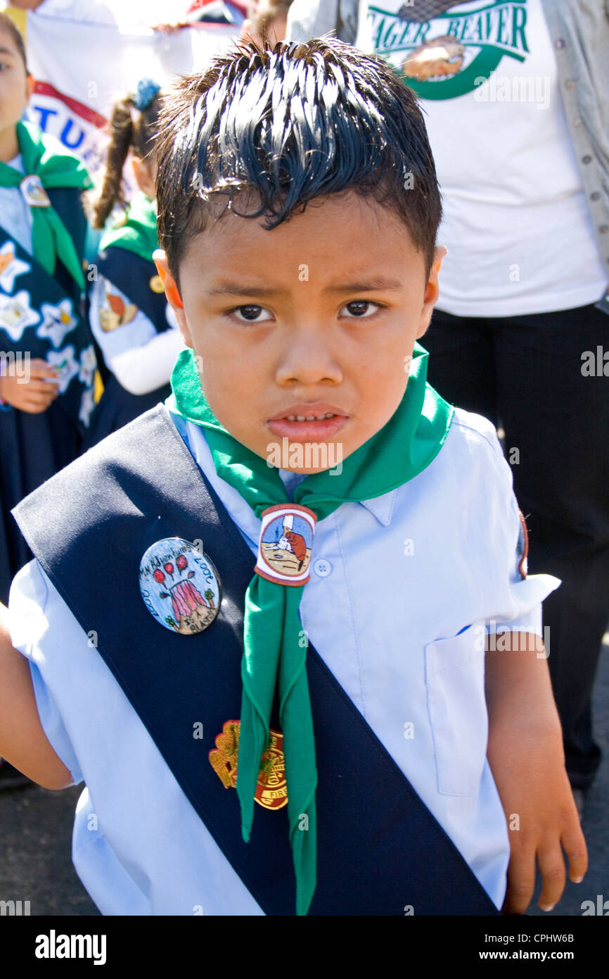 Young Mexican American Cub Scout wearing sash of merit badges in parade ...