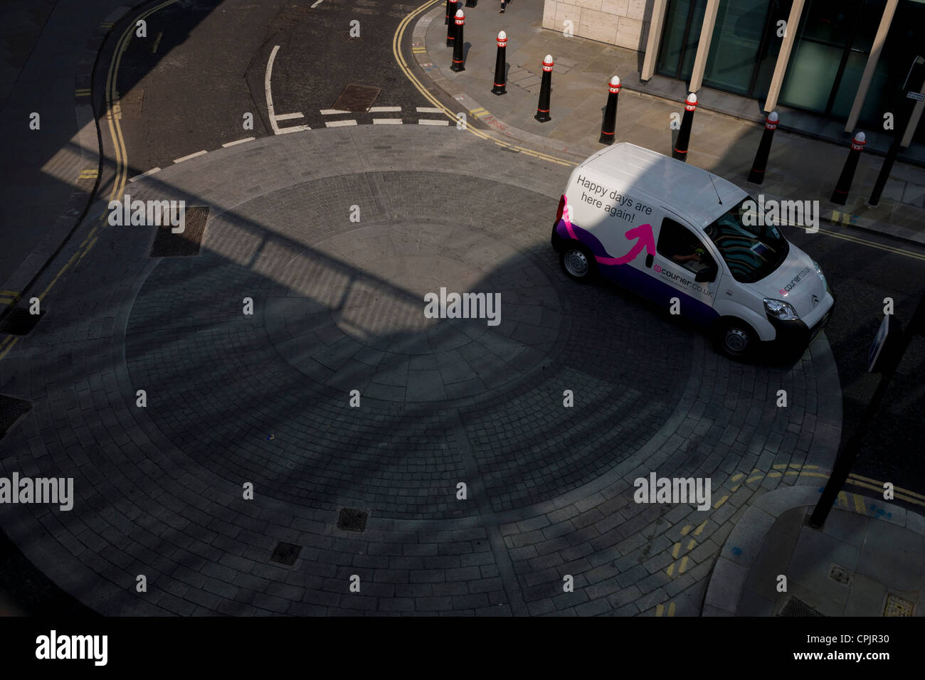 A white courier delivery van drives over a mini-roundabout in a City of ...