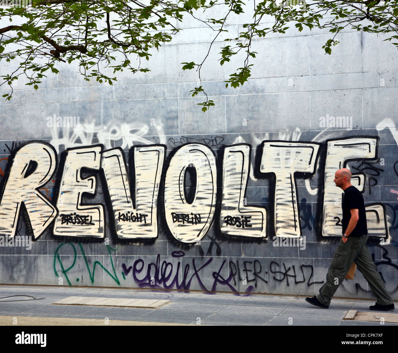 people passing by a large graffiti "revolte" on a wall Stock Photo - Alamy