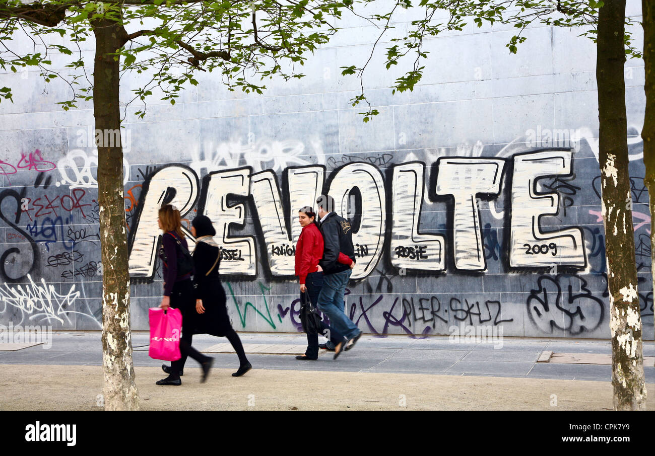 people passing by a large graffiti "revolte" on a wall Stock Photo - Alamy