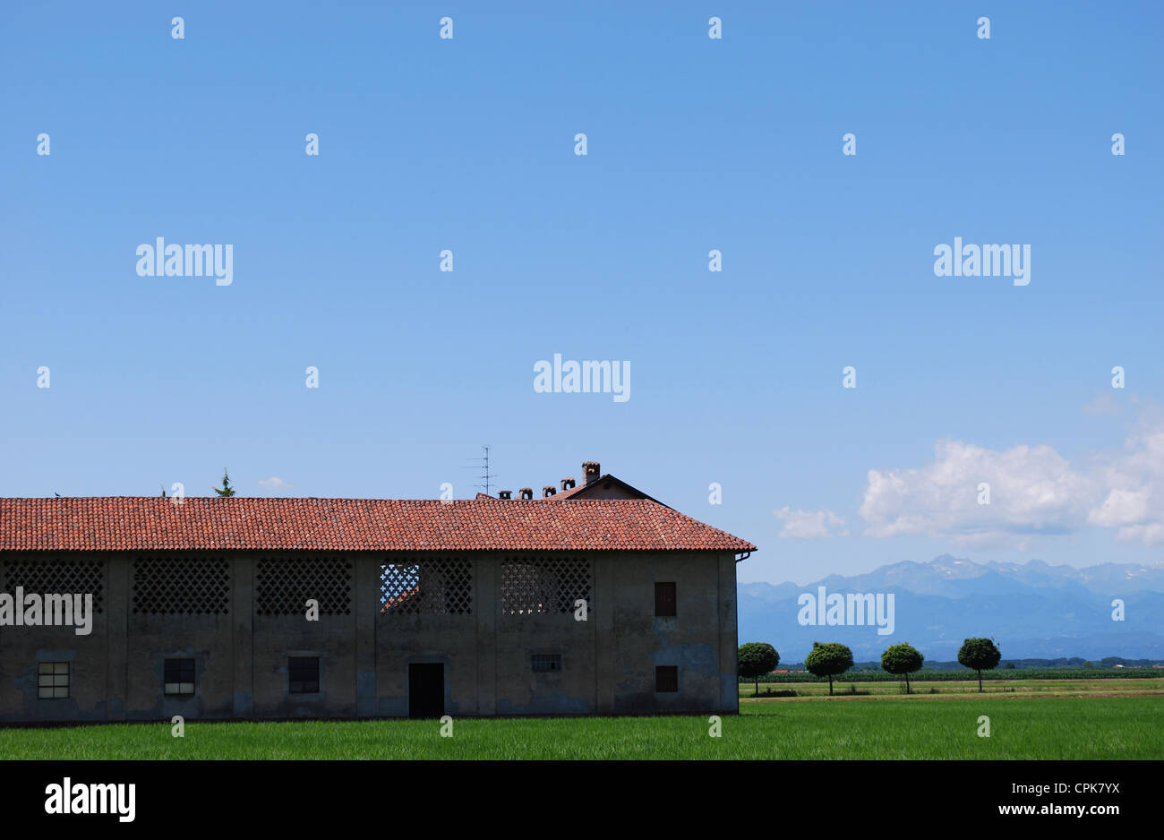 Farm house and flat farmland in summer, Alps mountains in background ...