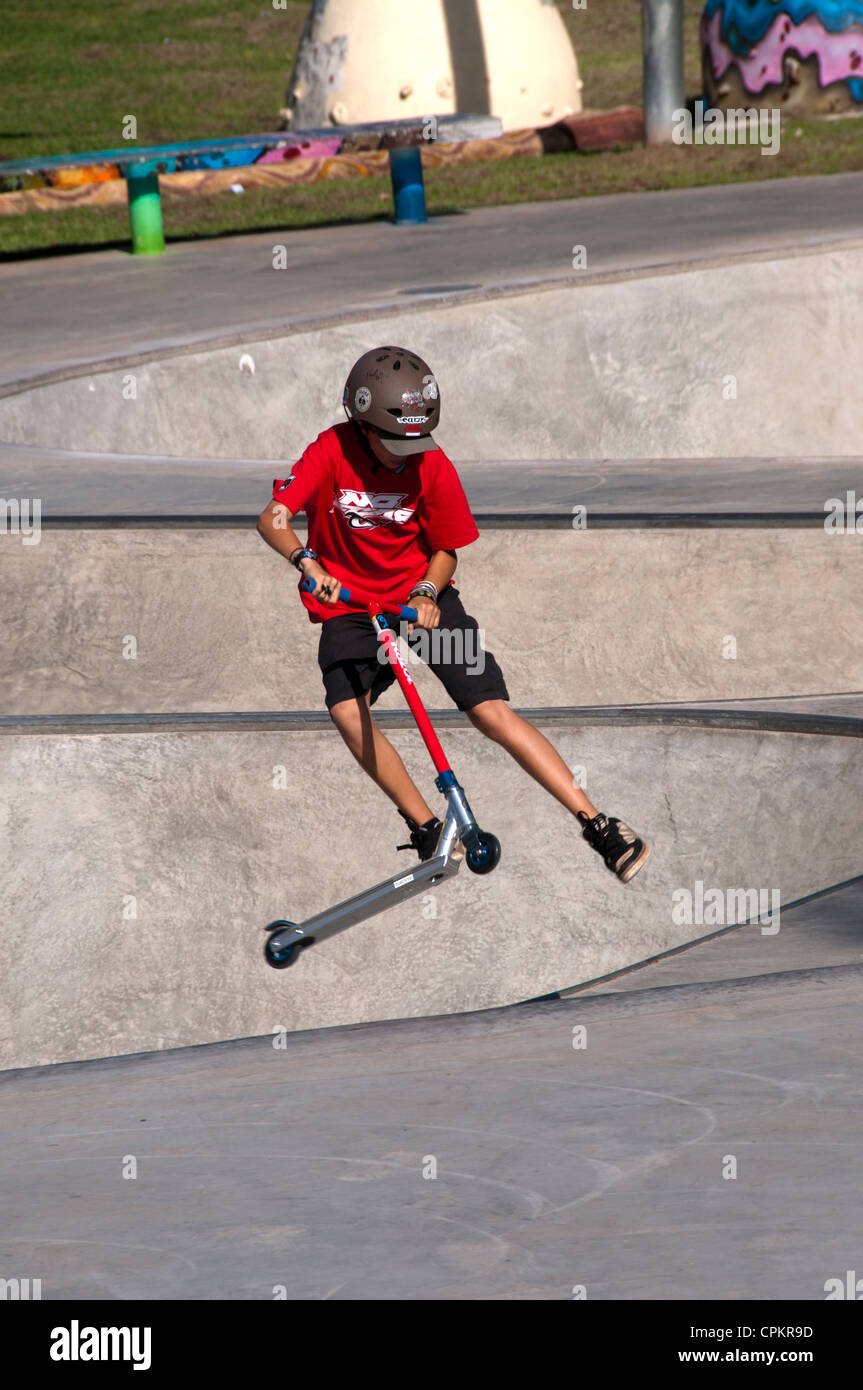 Young boy on a scooter does a jump in a purpose-designed skate park ...