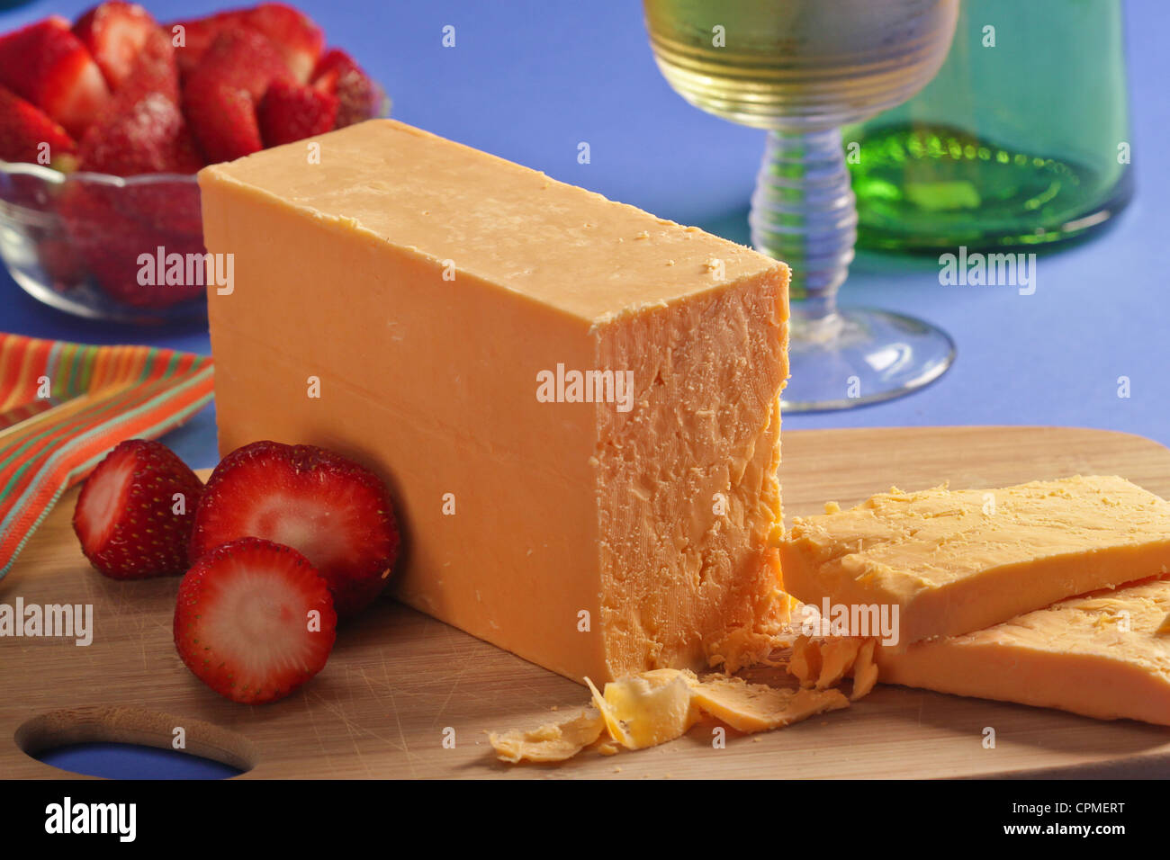 A block of aged yellow cheddar cheese sliced on cutting board with ...