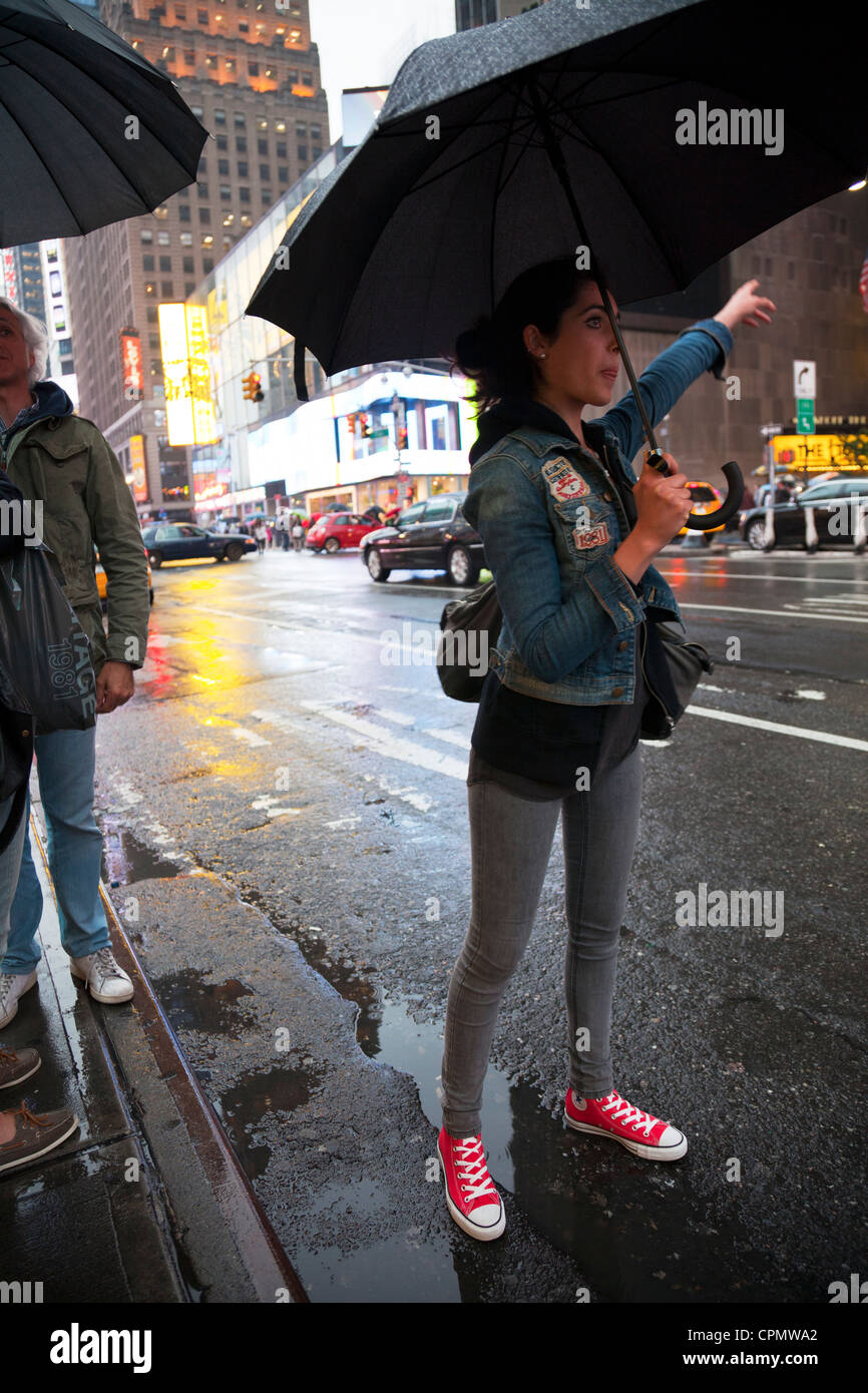 Young girl trying to hail, hailing a taxi cab in the rain in New York ...