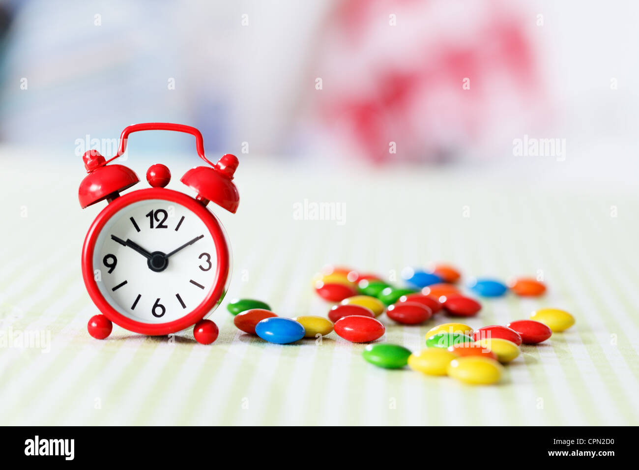 Small red alarm clock and multi-colored candies Stock Photo - Alamy