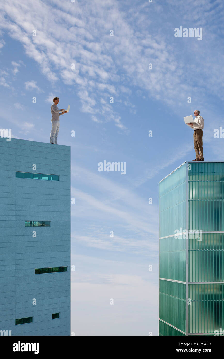 Men standing on top of high rise buildings, using laptop computers ...