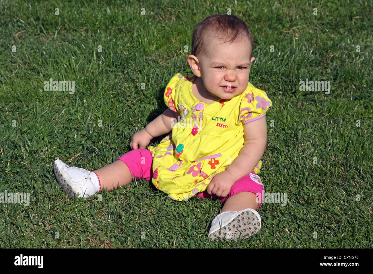 Frowning toddler girl in yellow dress and pink pants sitting down on ...
