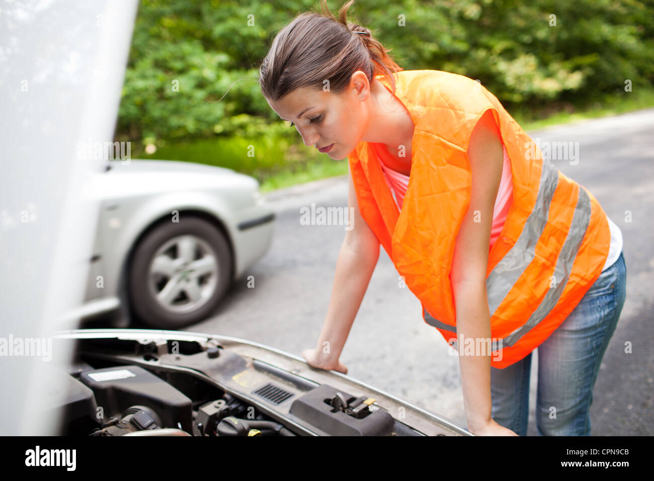 Young female driver wearing a high visibility vest, bending over the ...