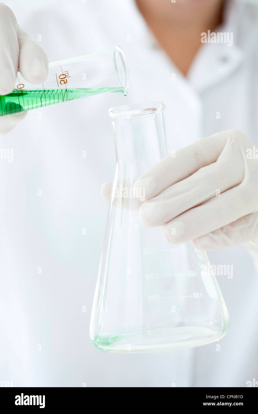 Scientist pouring liquid from graduated cylinder to conical flask Stock ...