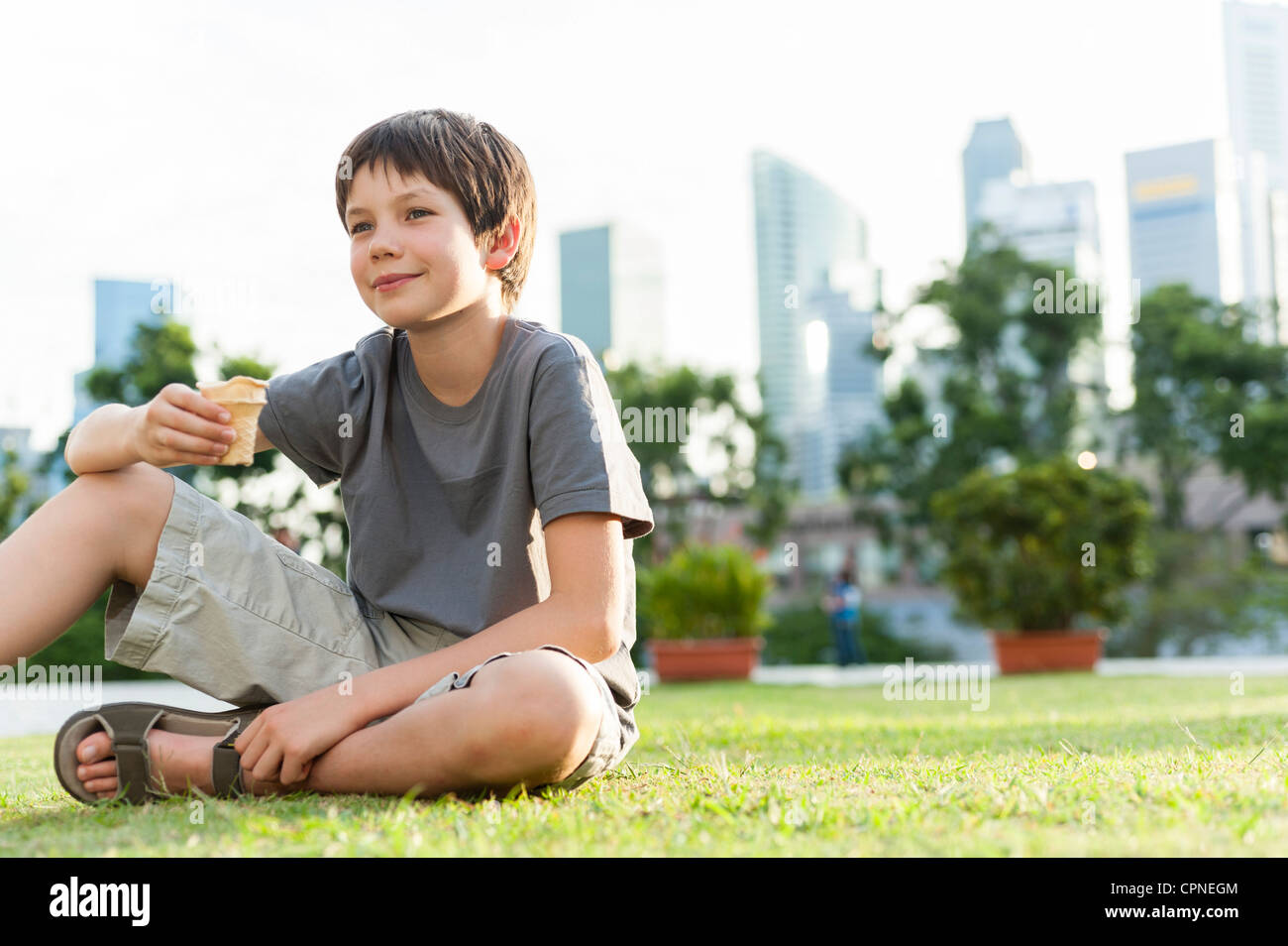 Boy sitting on grass in park, city skyline in background Stock Photo ...
