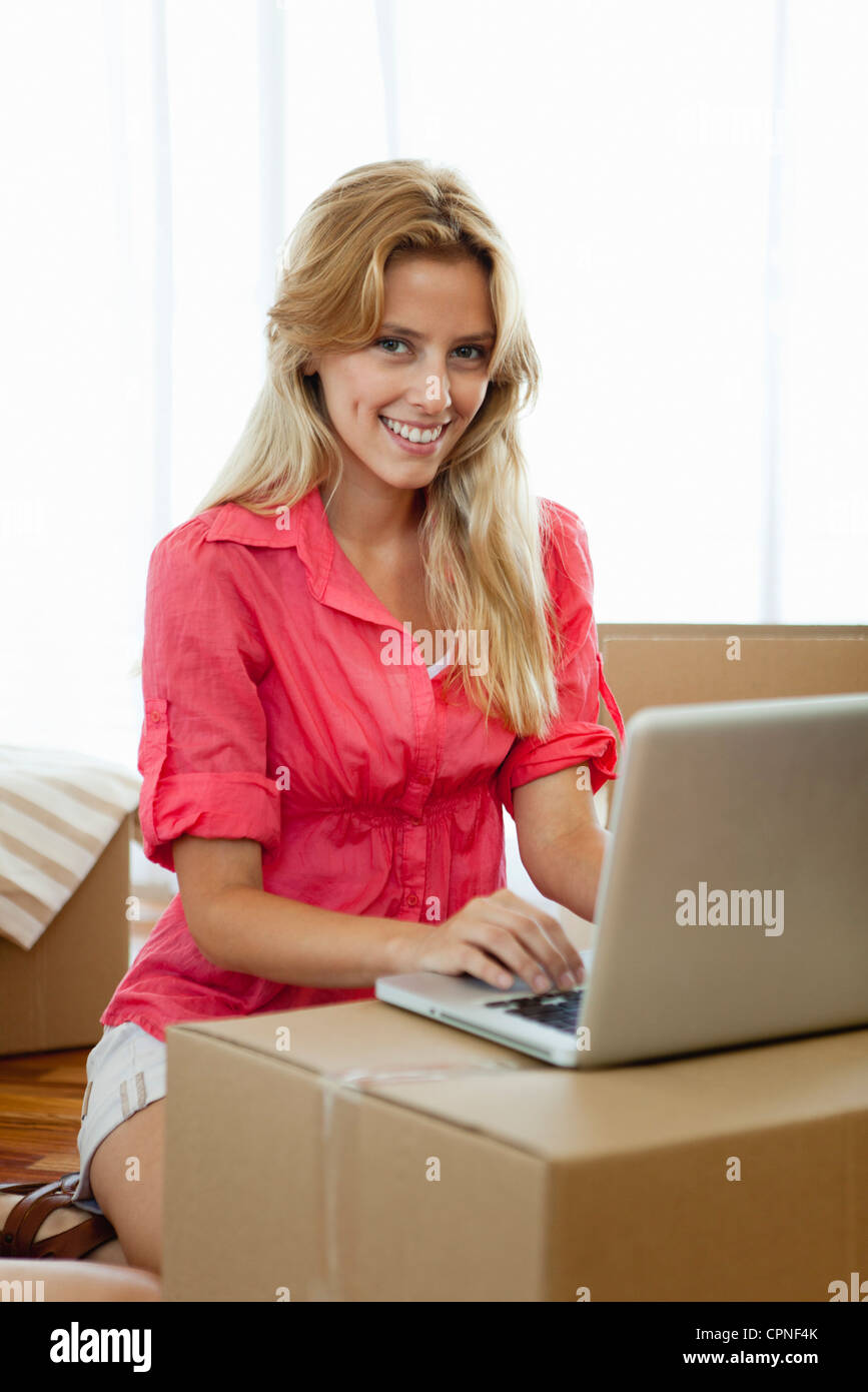 Young woman using laptop computer while surrounded by cardboard boxes ...