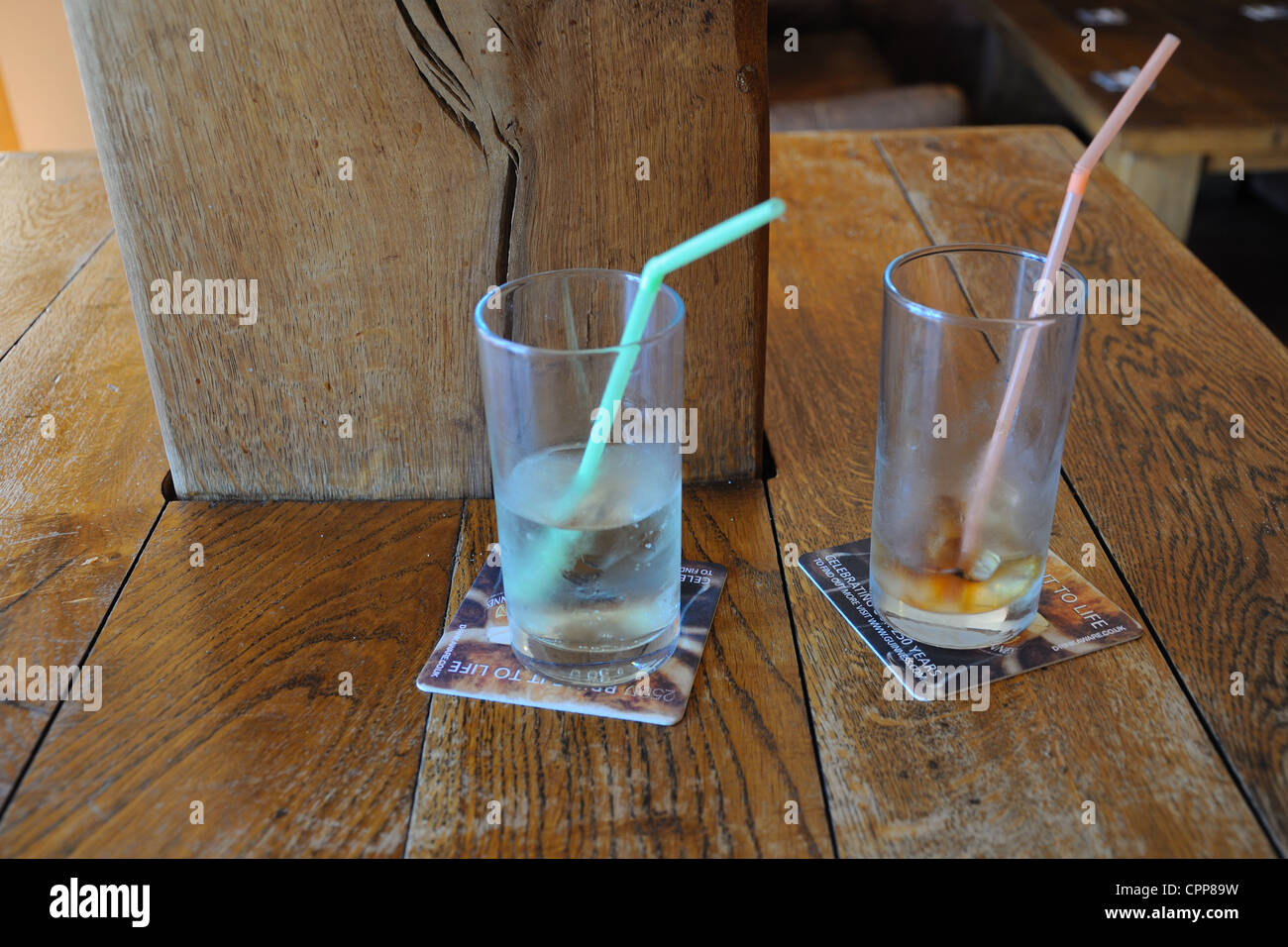 Two almost empty soft drinks glasses with straws on a solid wood table ...
