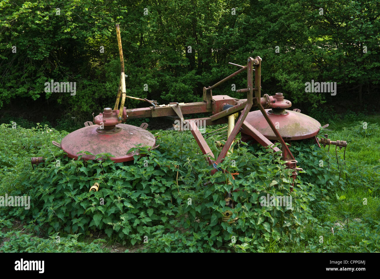 Old hay rake surrounded by nettles in a field on remote farm at ...