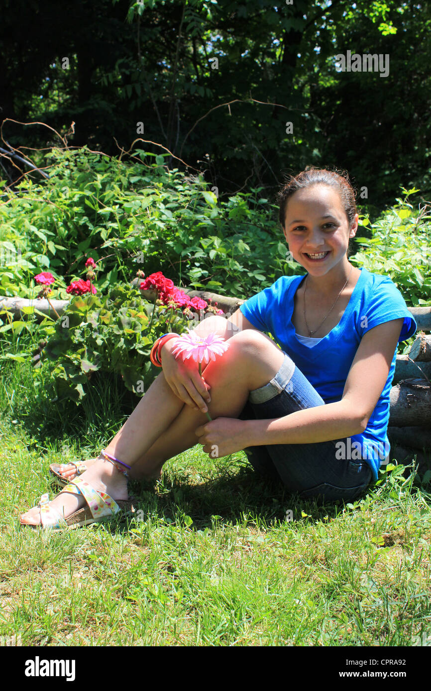 Pretty eleven year old girl holding a pink flower outdoors in the ...