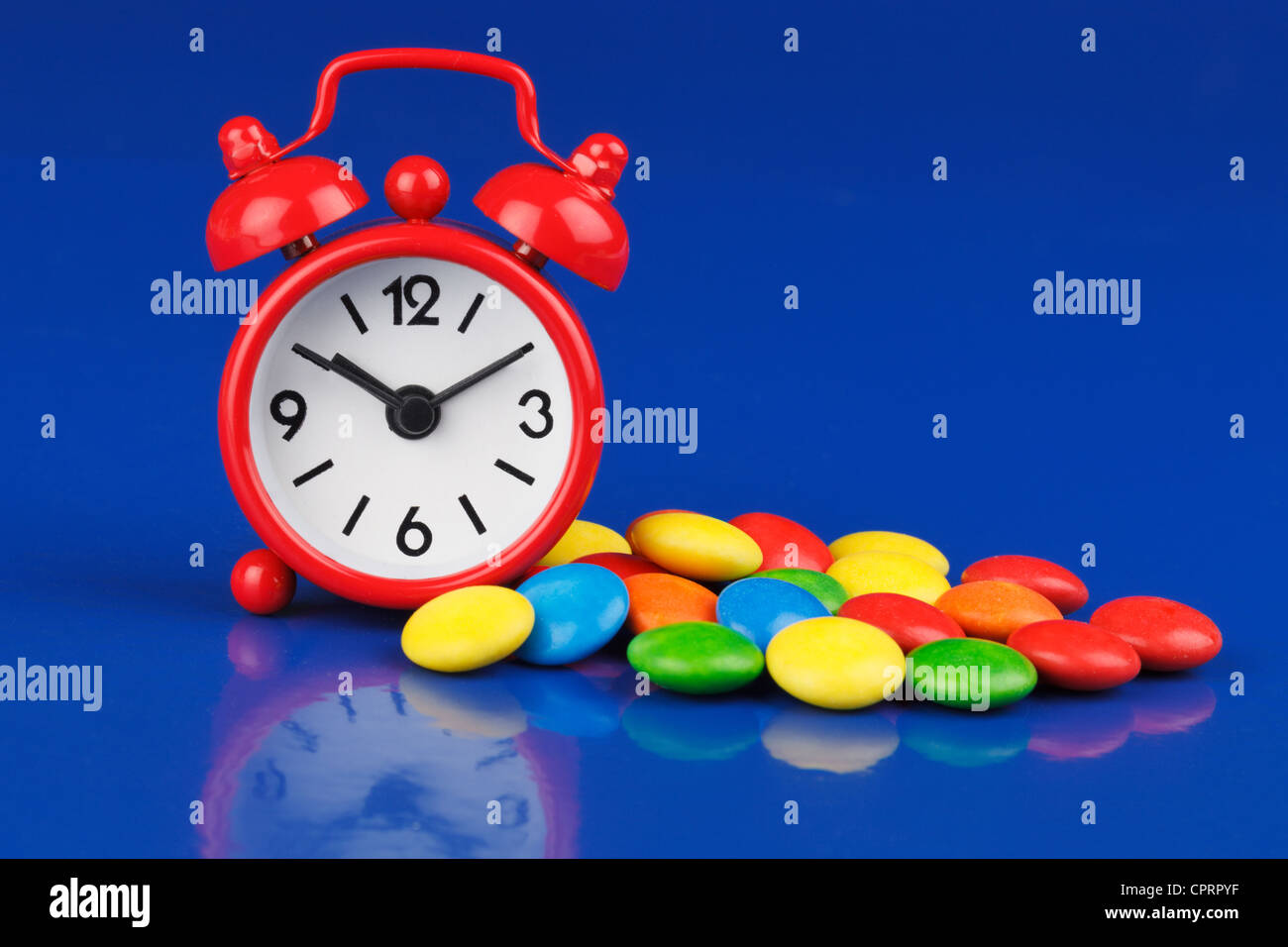 Small red alarm clock and multi-colored candies Stock Photo - Alamy