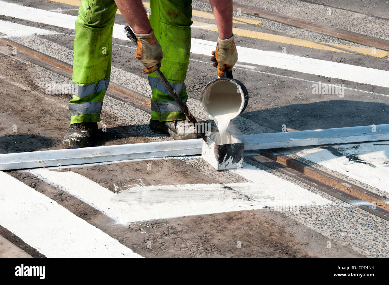 Workman using a screed box for marking a road surface next to a tram ...