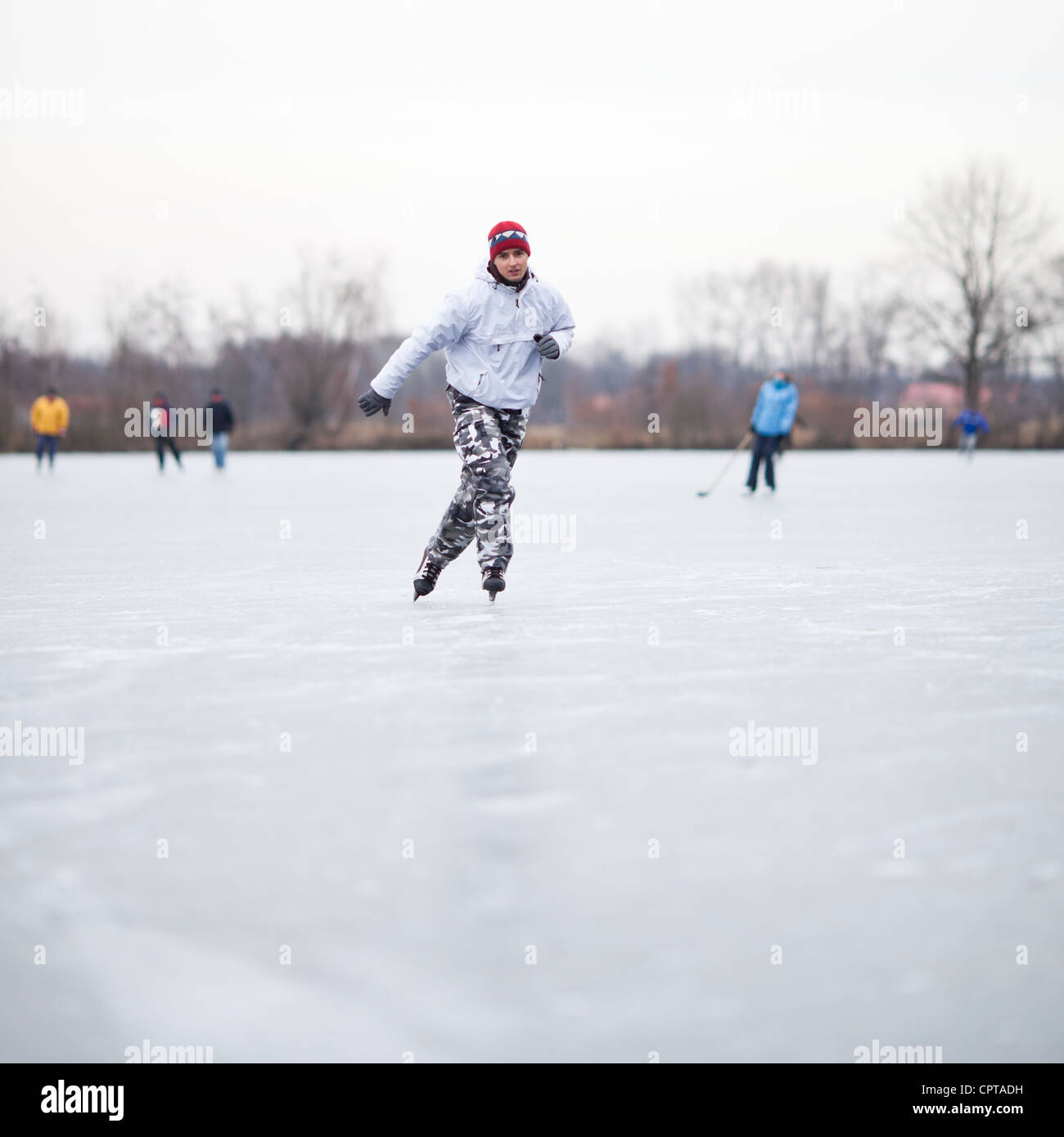 Handsome young man ice skating outdoors on a pond on a cloudy winter ...