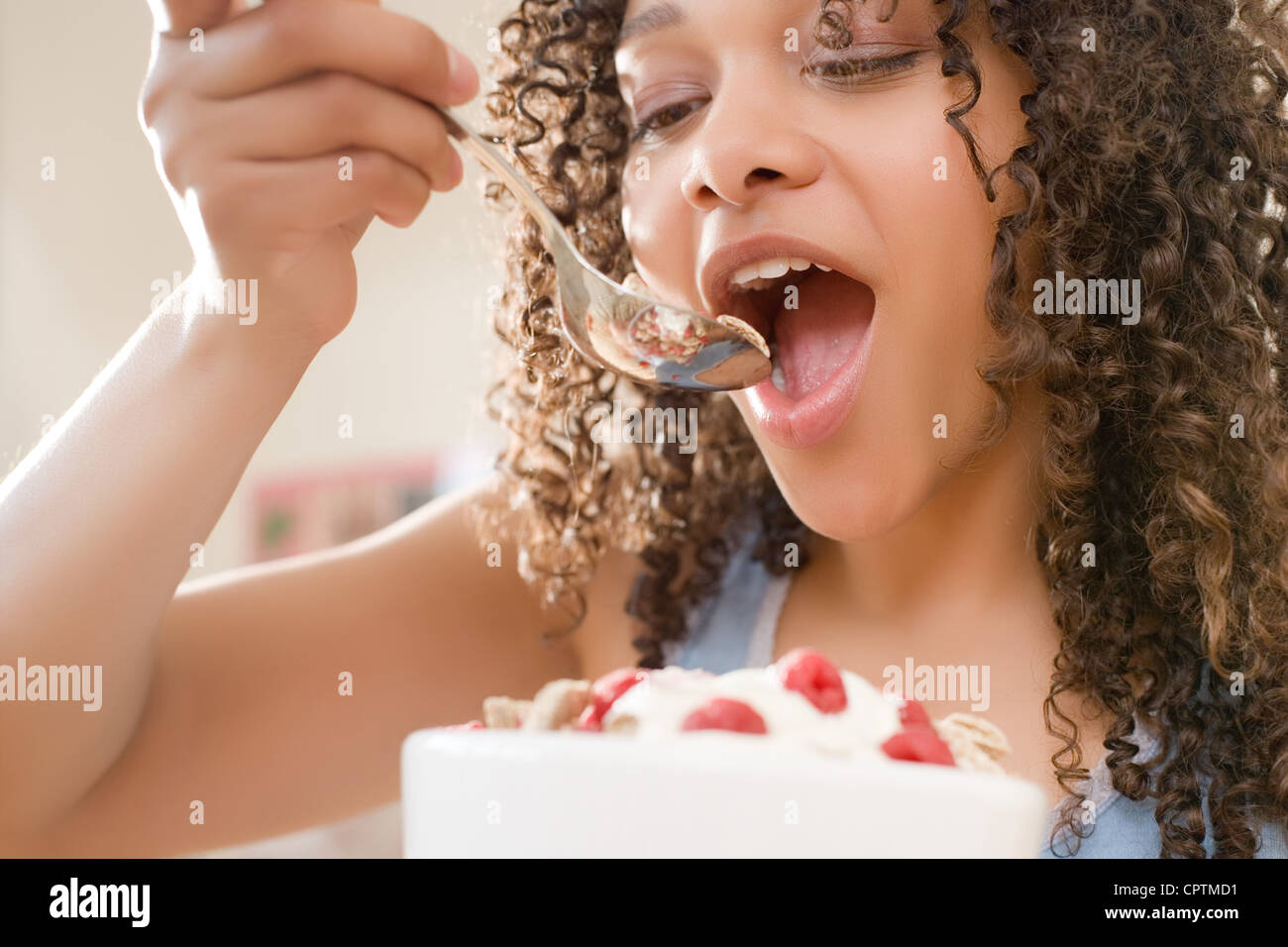 Young woman eating cereal yogurt and raspberry's from a breakfast bowl ...
