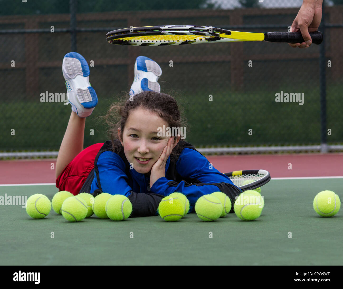 Young girl having fun on outdoor tennis courts with coach's racket ...