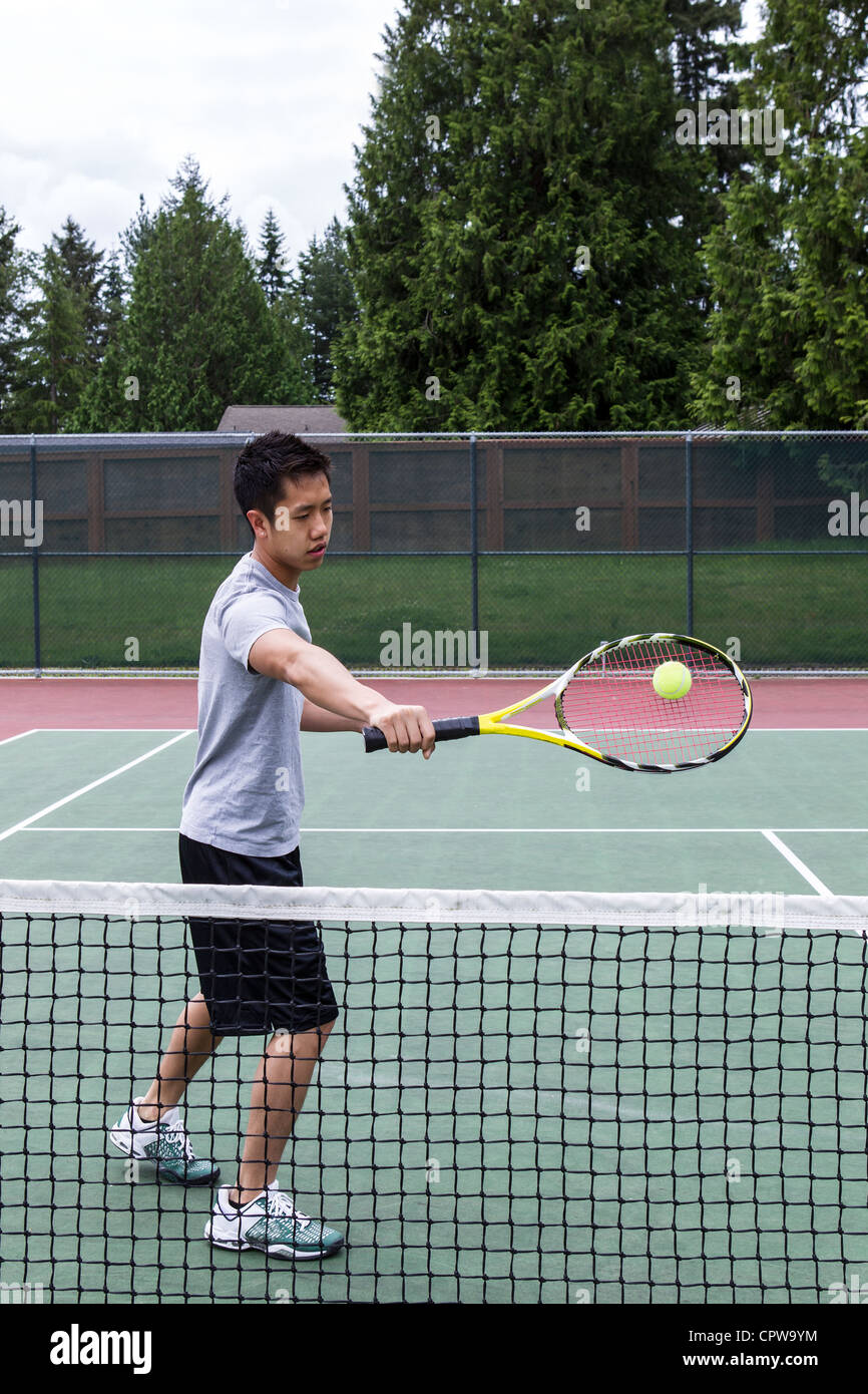 Young Asian Man using backhand volley on outdoor tennis court Stock ...