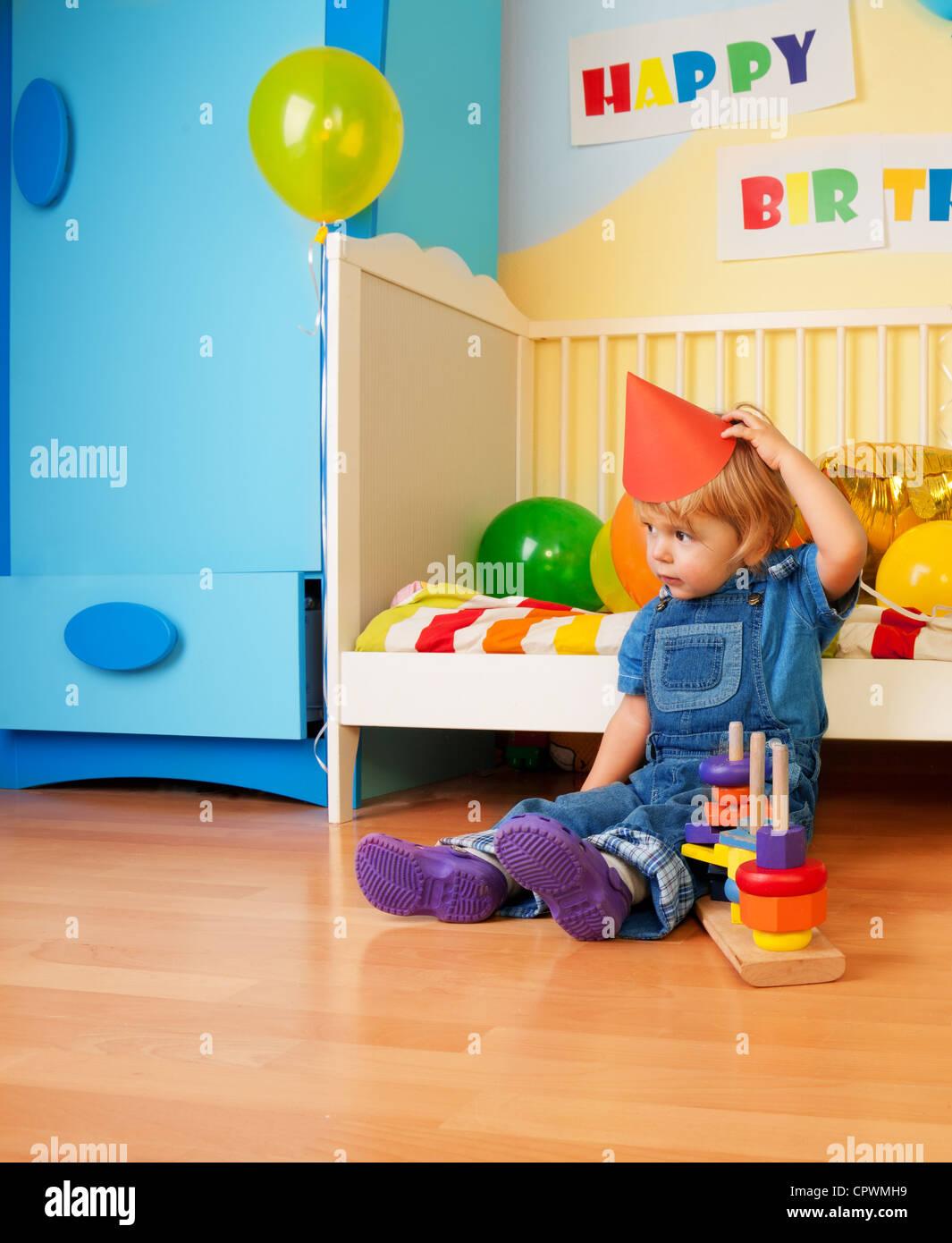 Surprised kid after birthday party sitting on the floor and holding cap ...