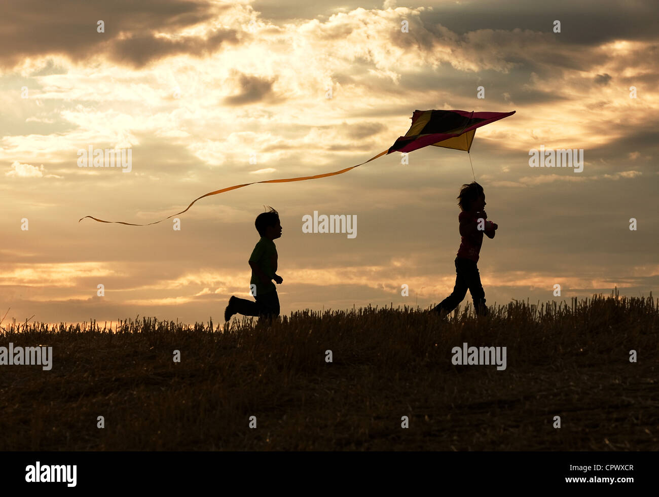 Two children enjoy flying a kite during sunset Stock Photo - Alamy