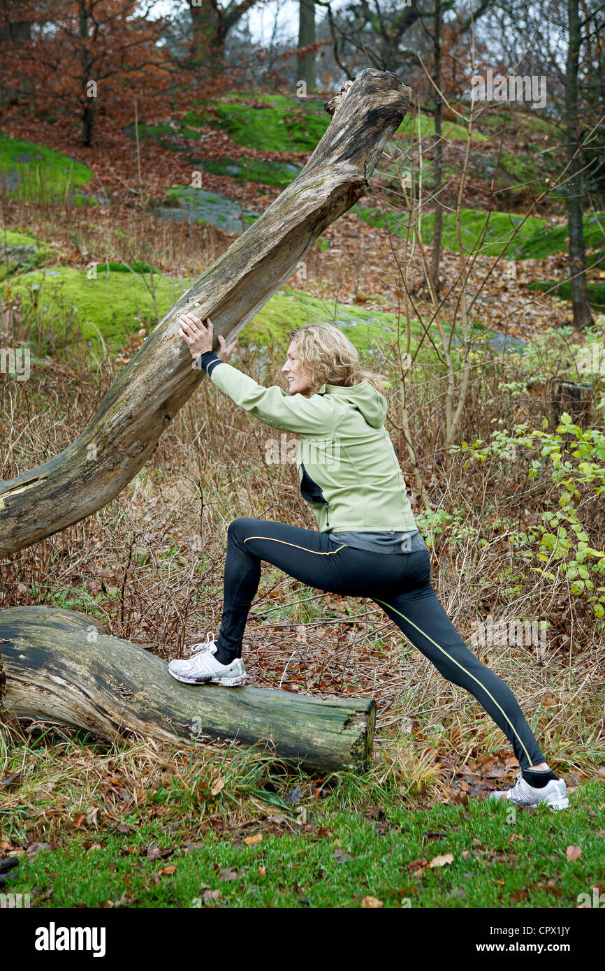 Mature woman stretching against tree in forest Stock Photo - Alamy