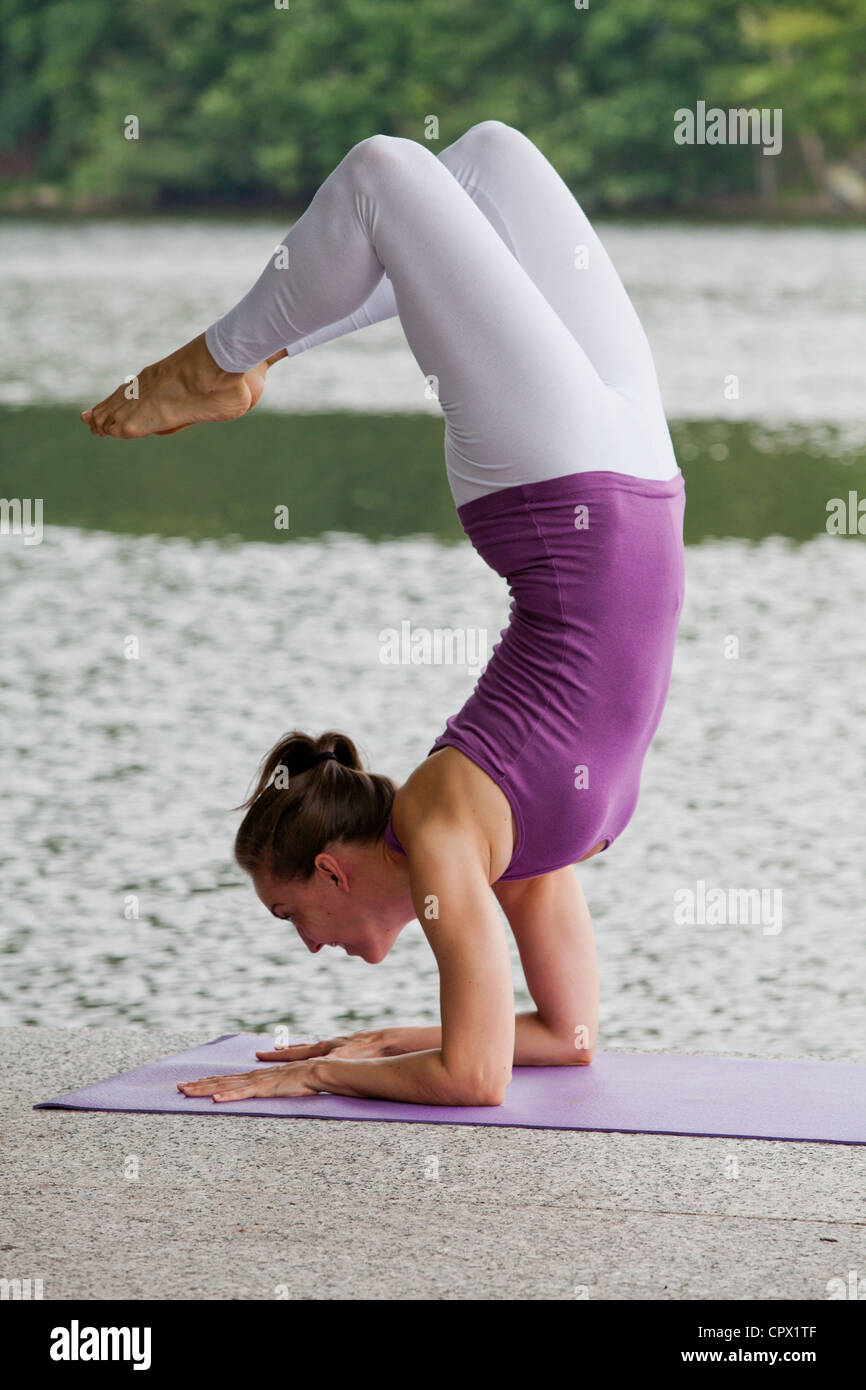Mid adult woman performing yoga scorpion pose by river, looking away ...