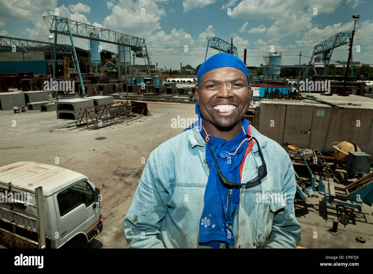 Black factory worker stands in construction yard smiling at camera ...