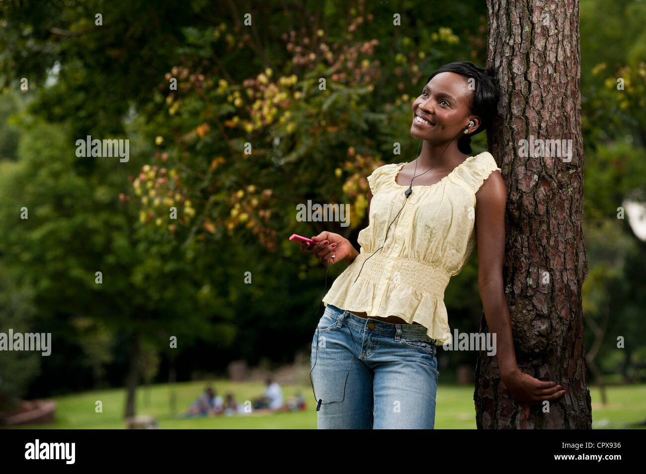 Young African woman standing against a tree in a park, smiling Stock ...