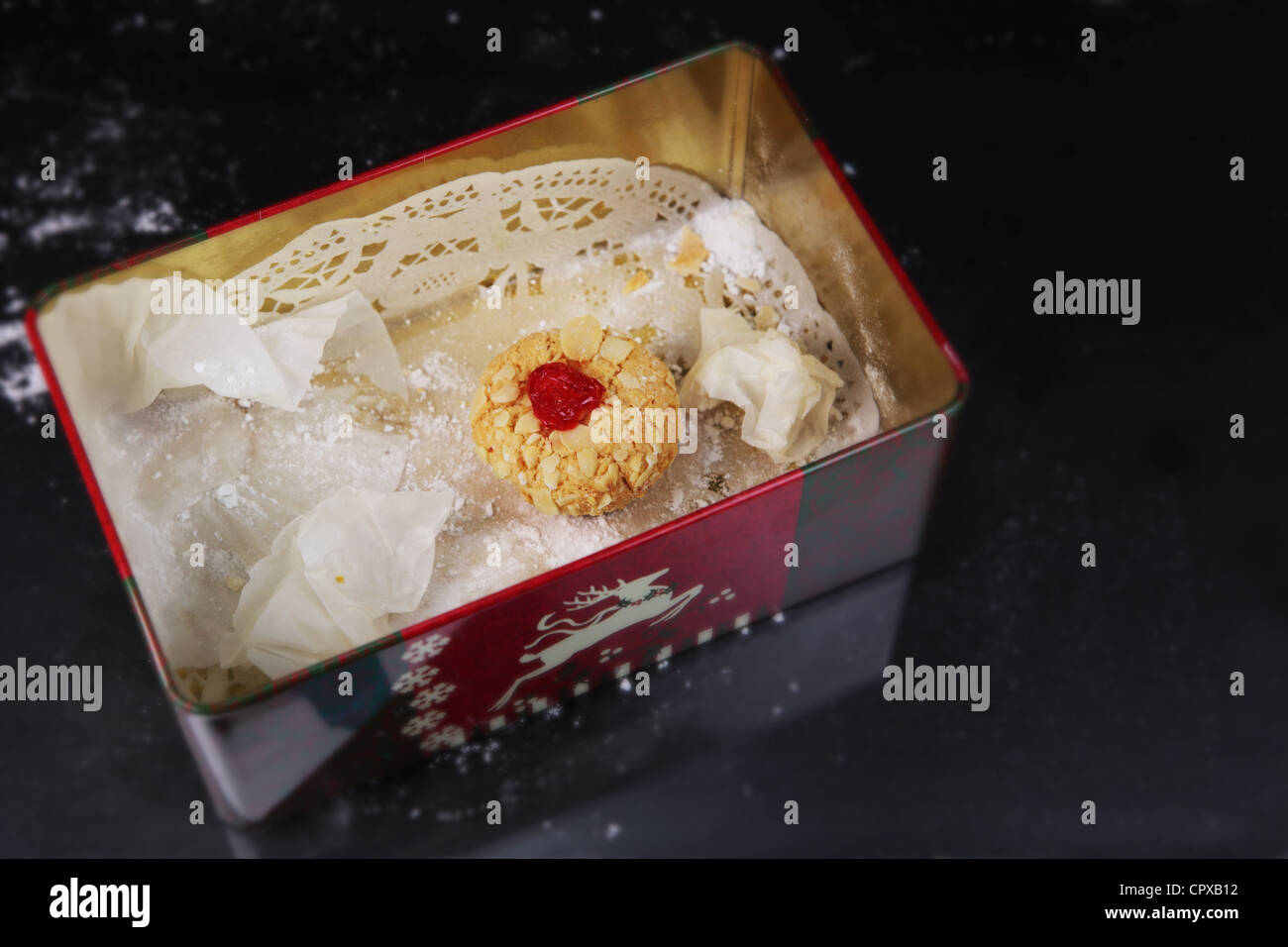 A cherry cookie left in a tin cookie box with a few empty cookie ...