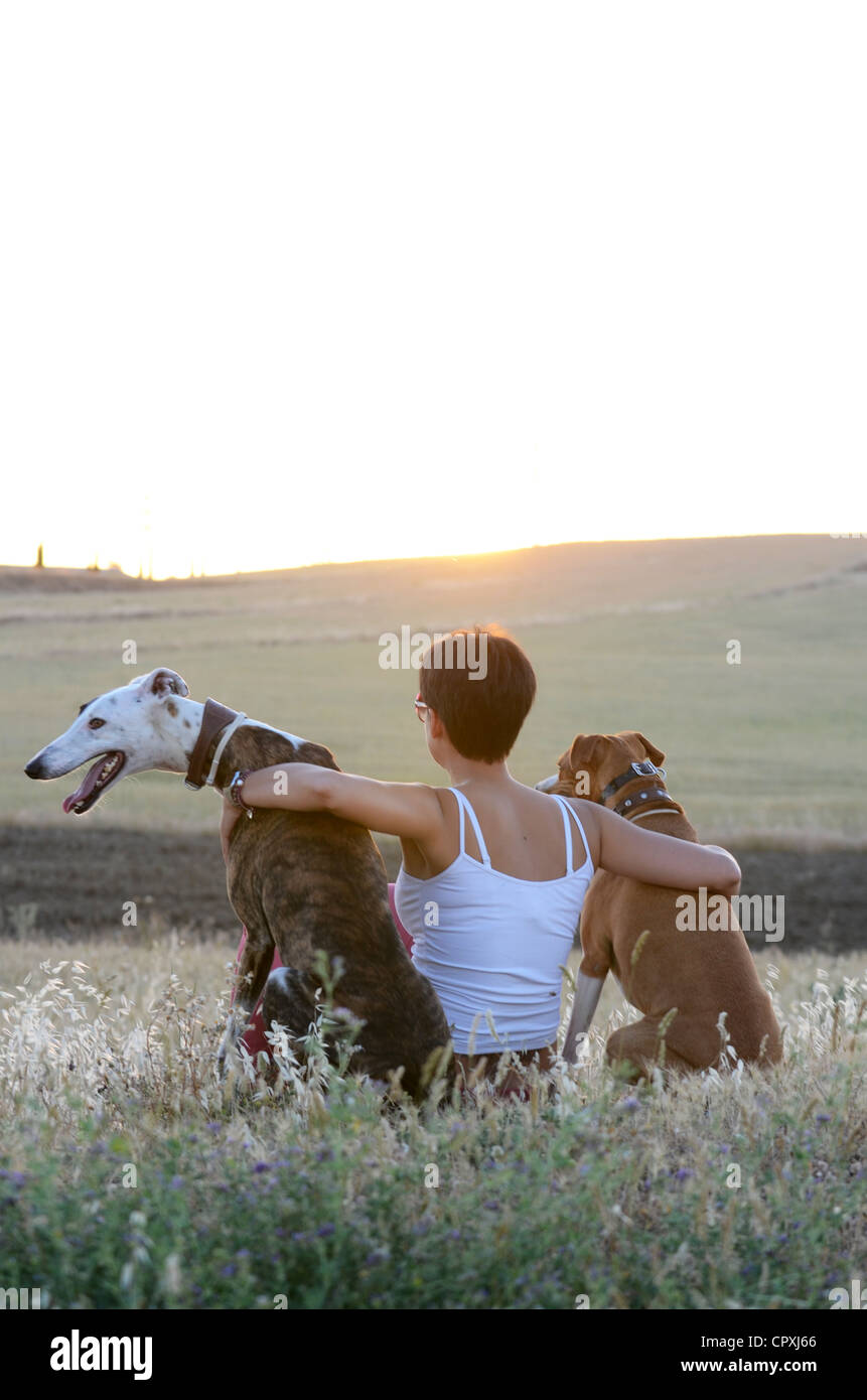 Young woman sitting in nature with her dogs, at sunset Stock Photo - Alamy