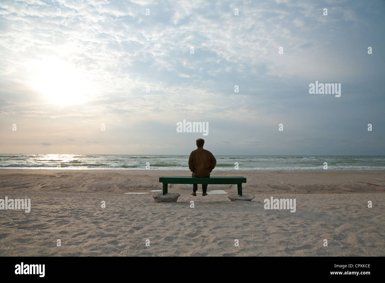 Adult man sitting alone on the bench looking at a stormy sea alone ...