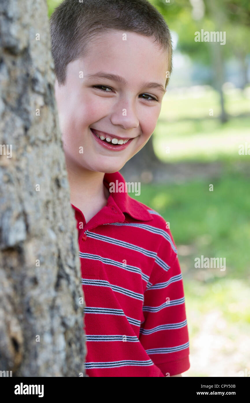 Caucasian boy smiling behind a tree in a park during summertime Stock ...