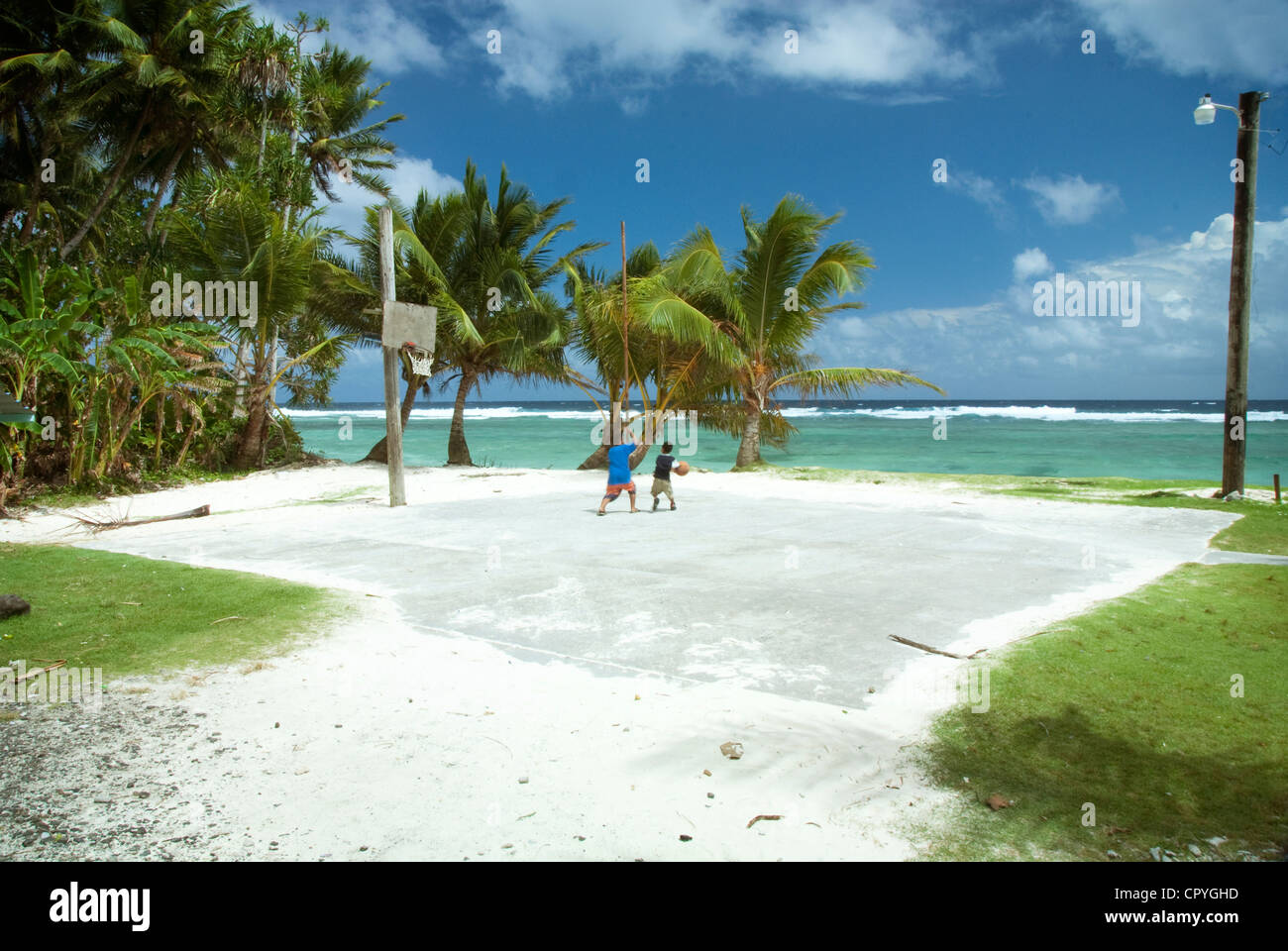 Two children play basketball on a court that wears the harsh tropical ...
