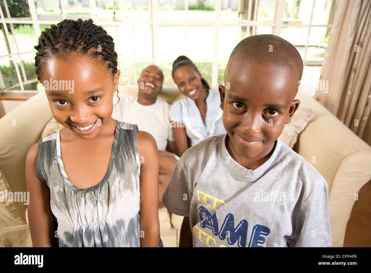 Two young African siblings smiling at camera, with their parents ...