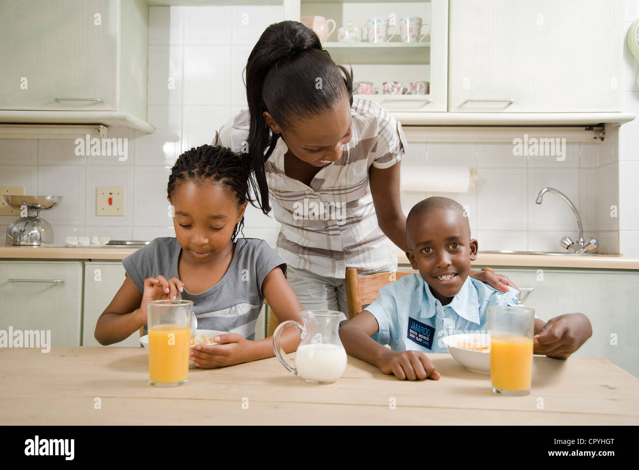Young African siblings eat breakfast together in a kitchen, with their ...