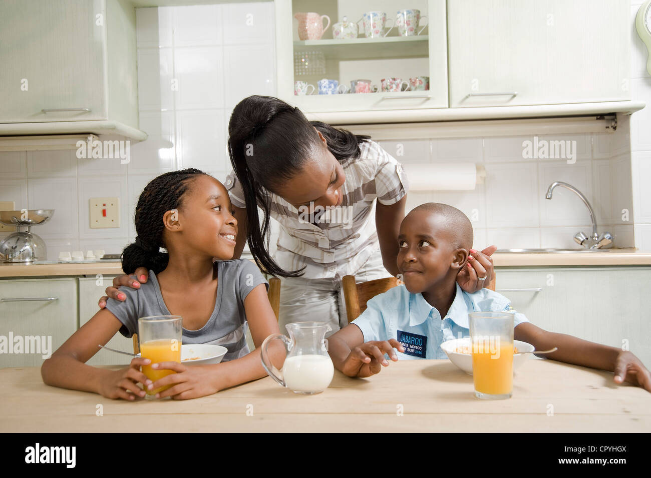 Young African siblings eat breakfast together in a kitchen, with their ...
