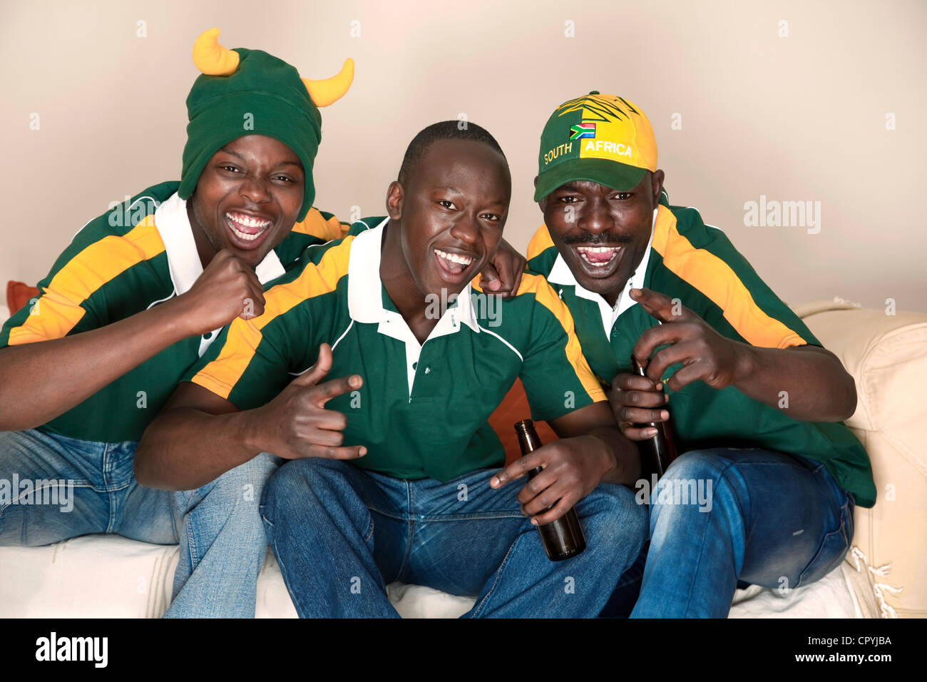 Three friends dressed in rugby uniforms watch a rugby game on TV whilst ...