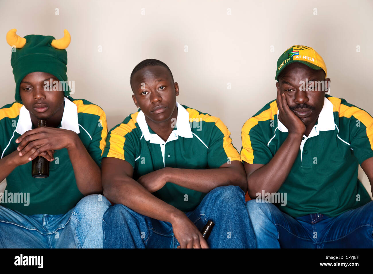 Three friends dressed in rugby uniforms watch a rugby game on TV whilst ...