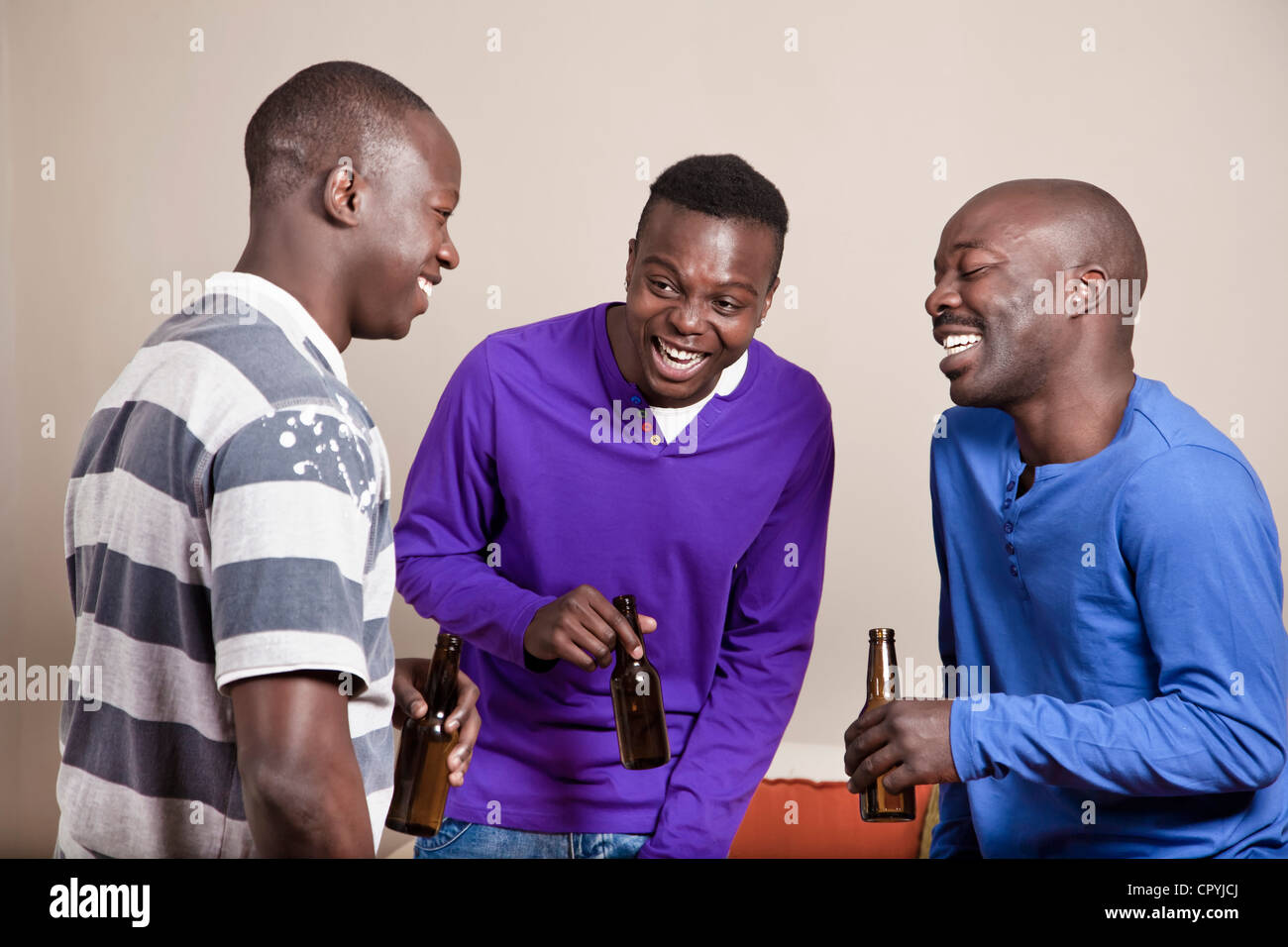 Three friends standing in a lounge, drinking beer and chatting Stock ...