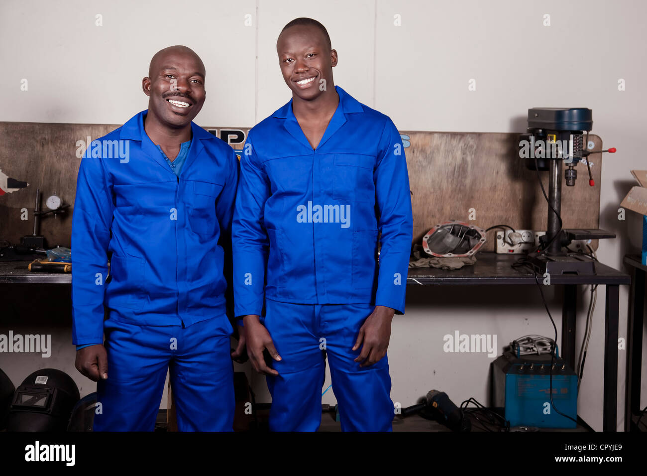 Two African mechanics standing in a workshop smiling at the camera ...